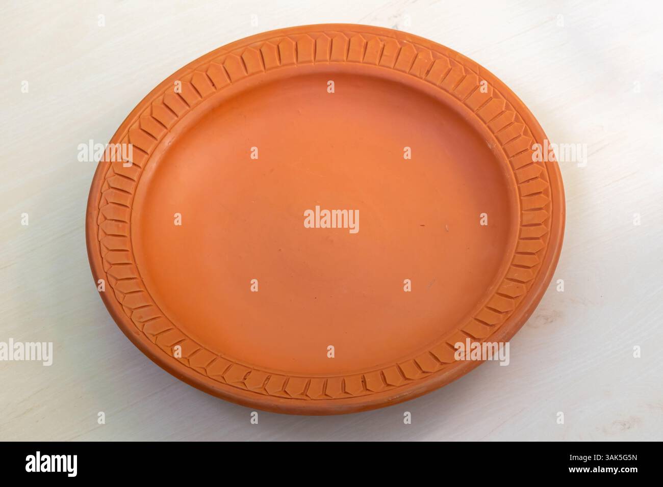 A traditional clay plate with a simple design on a light wooden surface ...