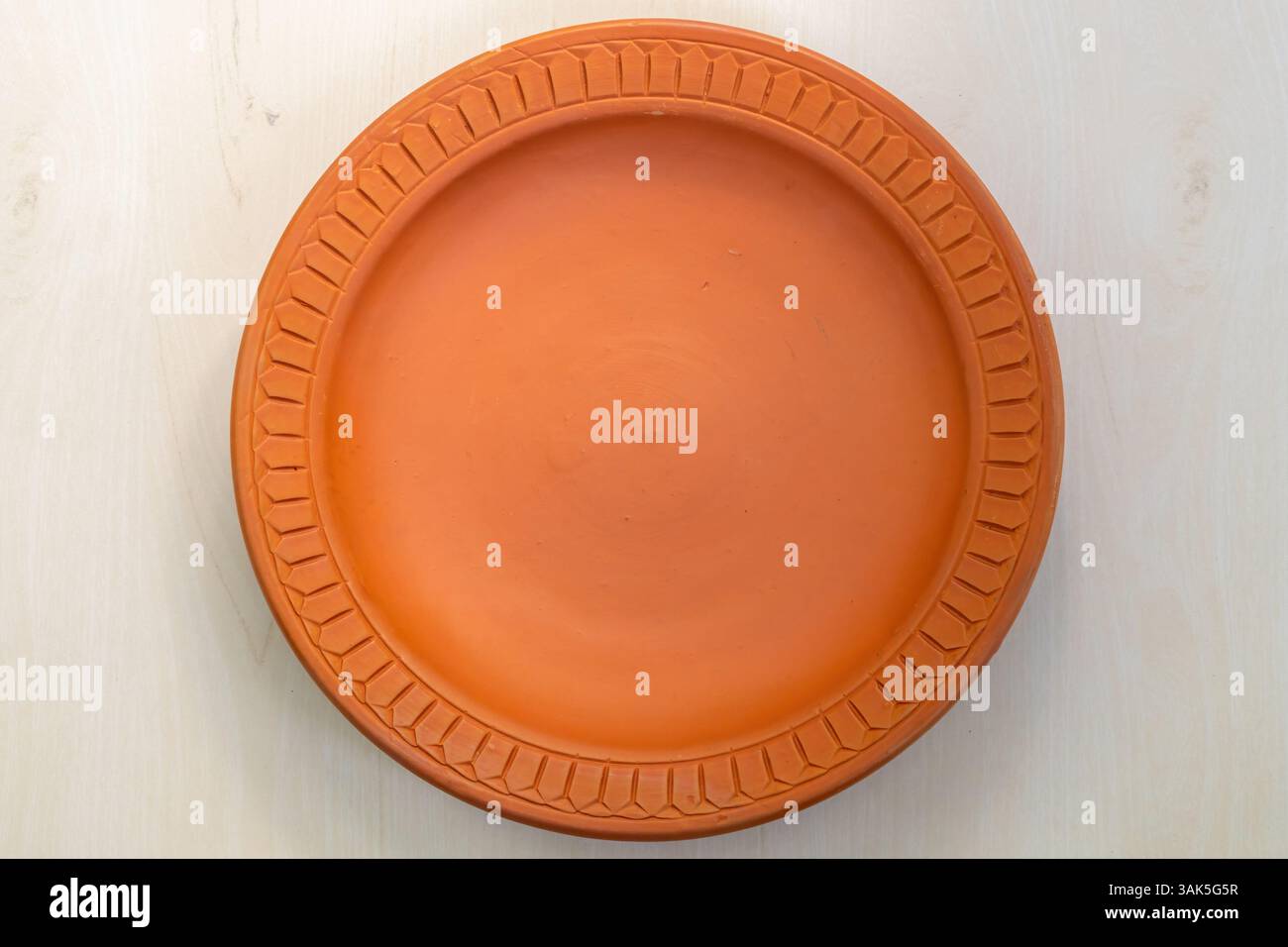 Traditional clay plate with a simple design on a light wooden surface ...