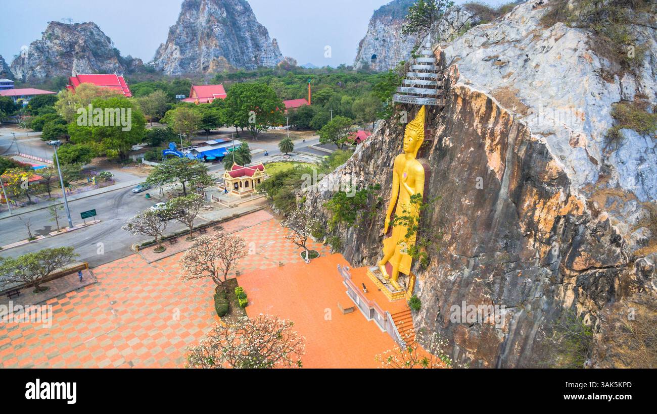 A majestic standing golden Buddha statue is carved into a rocky ...