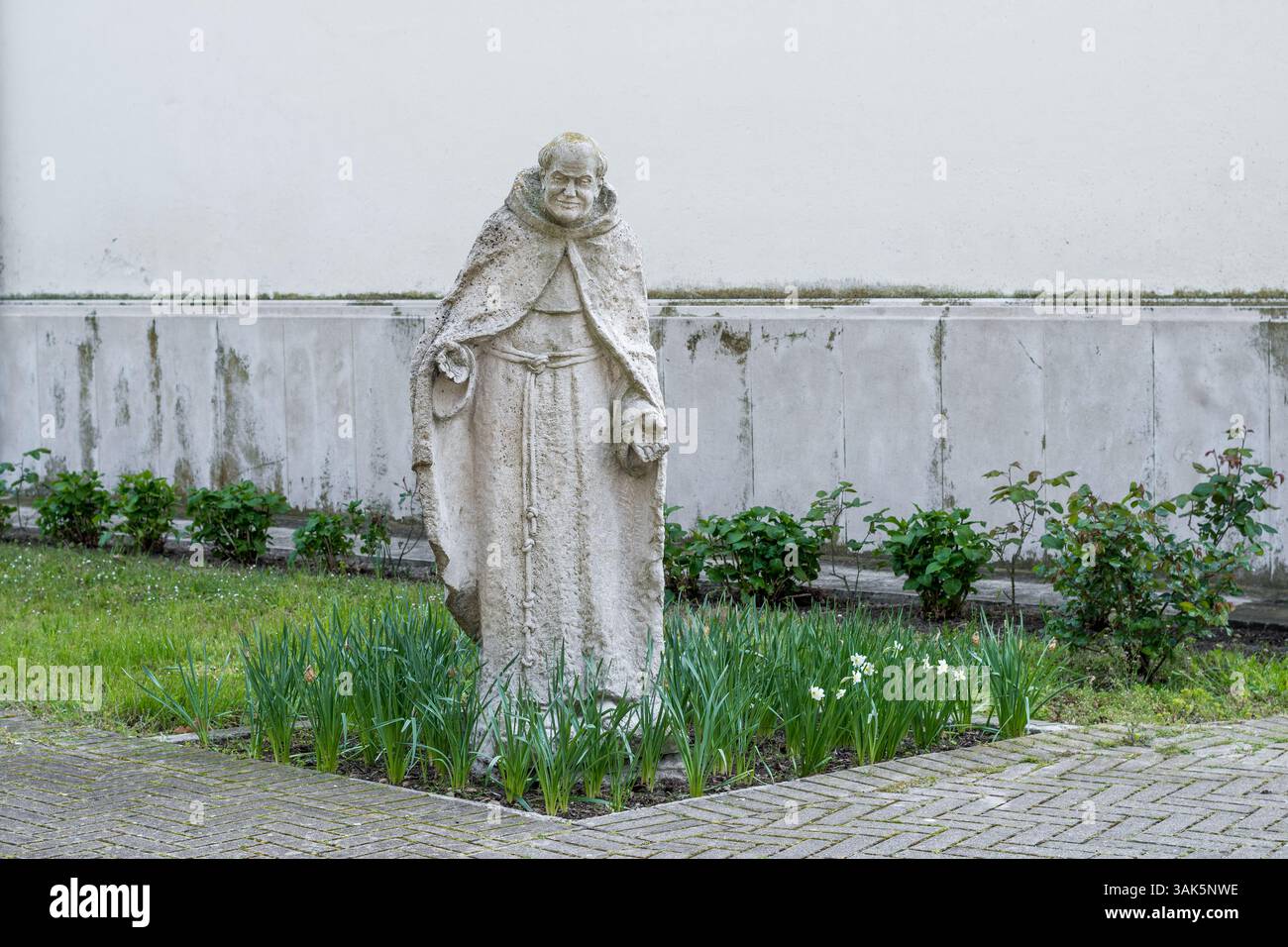 Ancient stone statue of a hooded monk standing peacefully among flowers ...