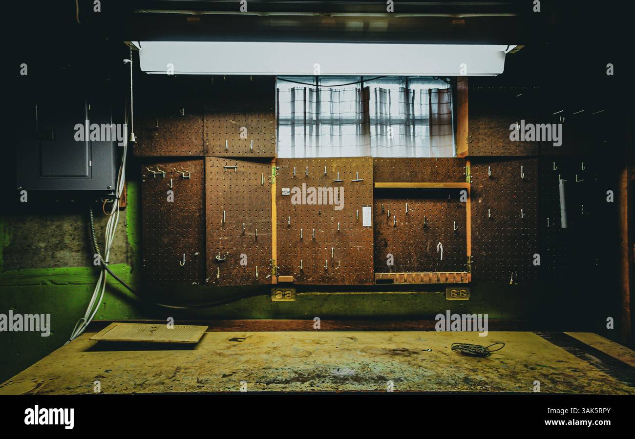 Grungy, industrial tool wall with empty hooks and a weathered workbench ...