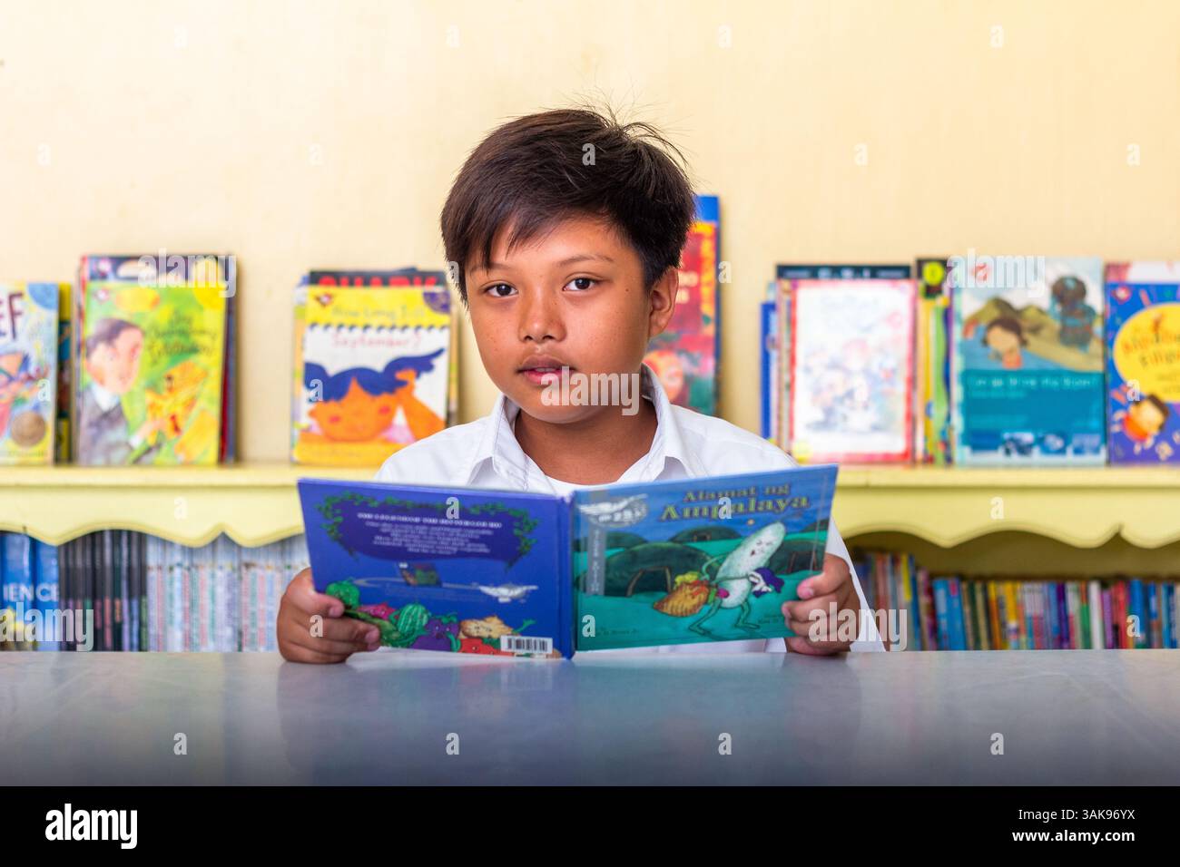 A young Filipino student reading a children's book inside a public ...