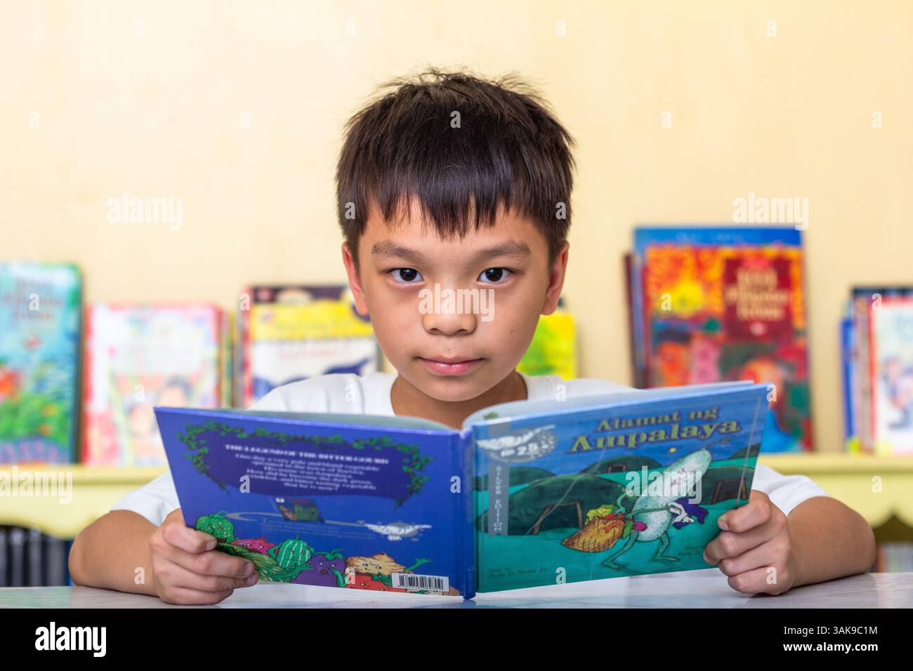 A young Filipino student reading a children's book inside a public ...