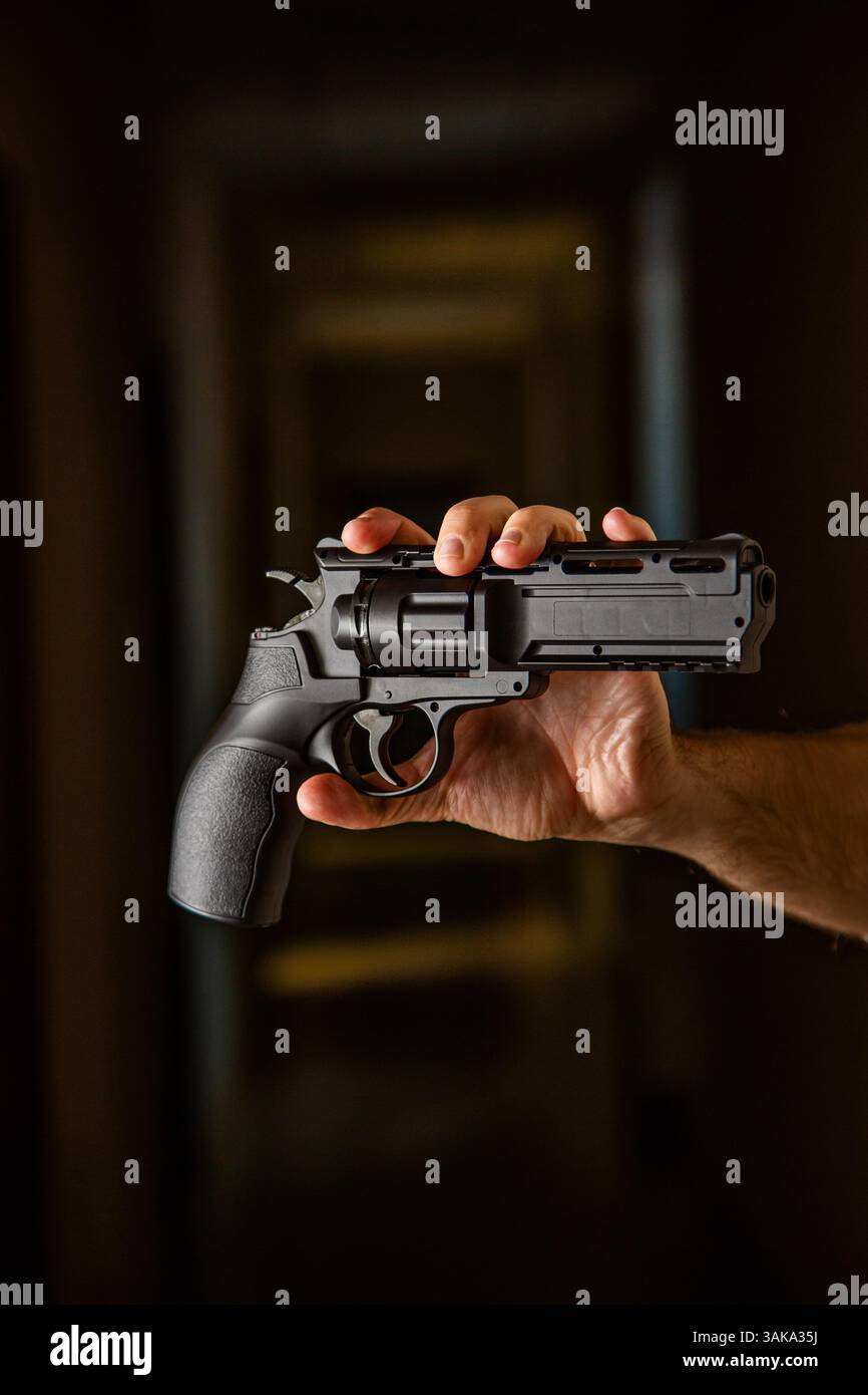 Black air pistol held in hand, side view in dark corridor, dramatic ...