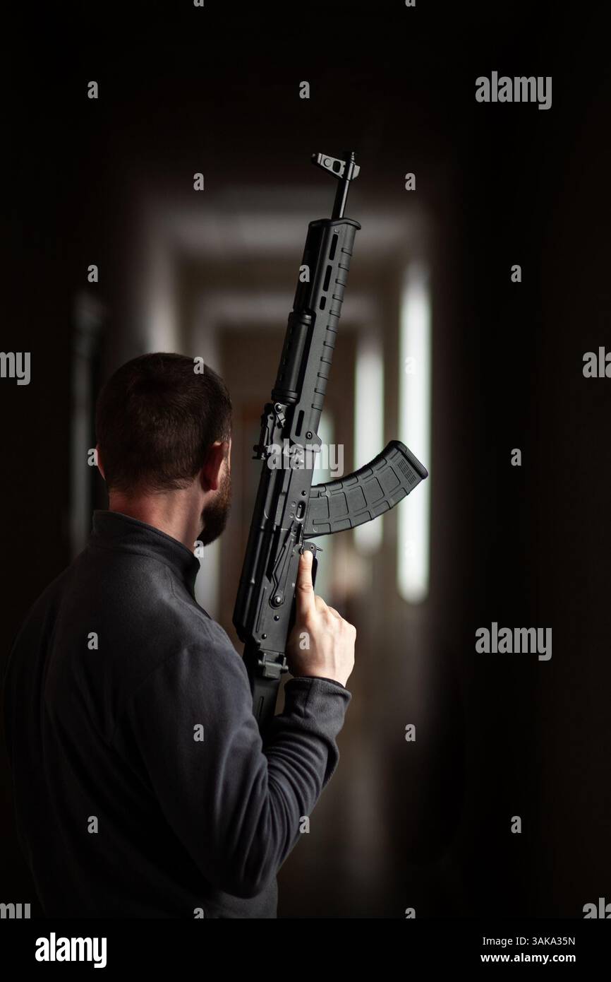 Man holding black tactical rifle indoors, back view in dim hallway ...