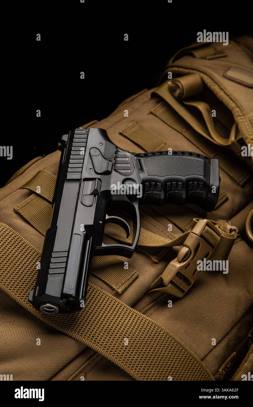Black tactical pistol resting on brown military backpack, top-down view ...