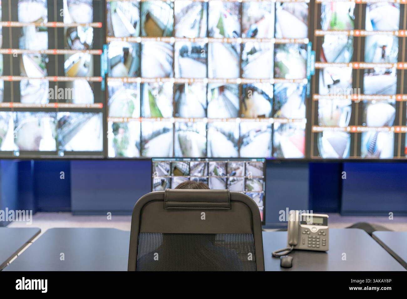 Security officer monitoring multiple surveillance screens in a high-tech control room for safety ...