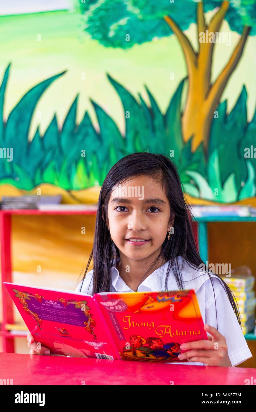 A young Filipino student reading a children's book inside a public ...