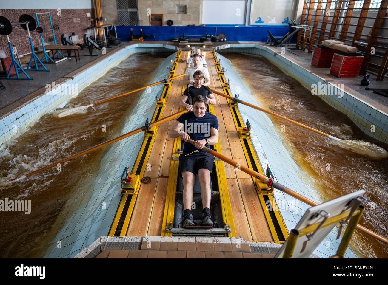 Concentrated tired athletes stroking on rowing simulator ...