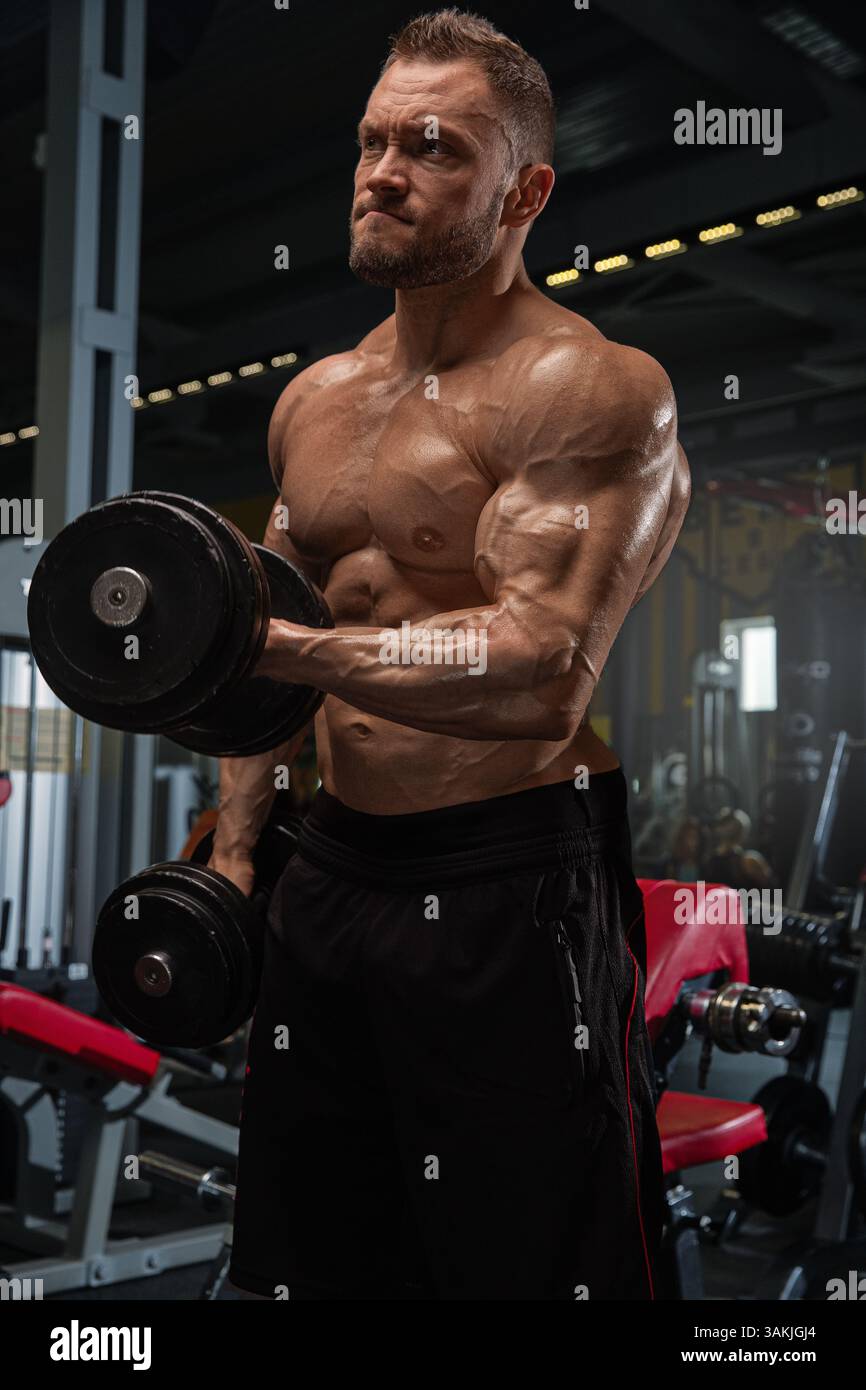 athletic man exercises dumbbells in well equipped gym. He showcases ...