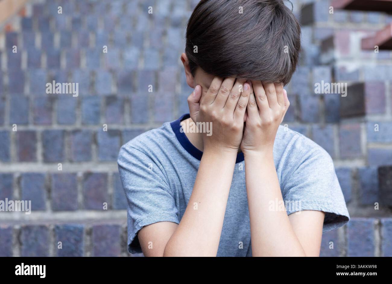 Sitting on stairs, boy covering face with hands, feeling upset at ...