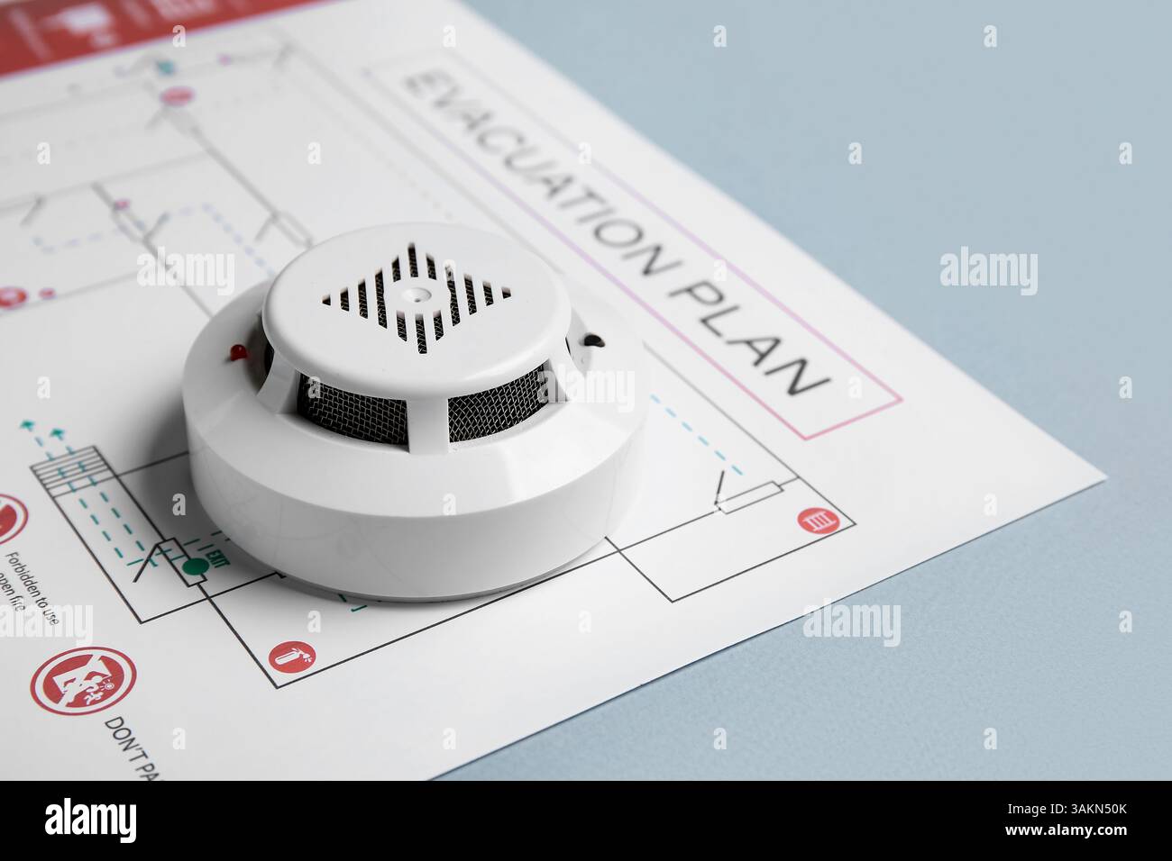 Modern smoke detector with evacuation plan on grey background, closeup ...