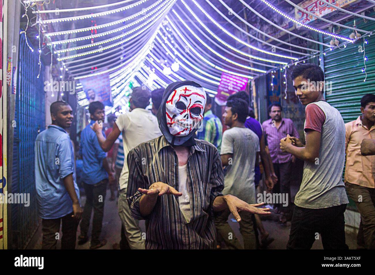 A masked youth poses playfully under festival lights during a lively ...