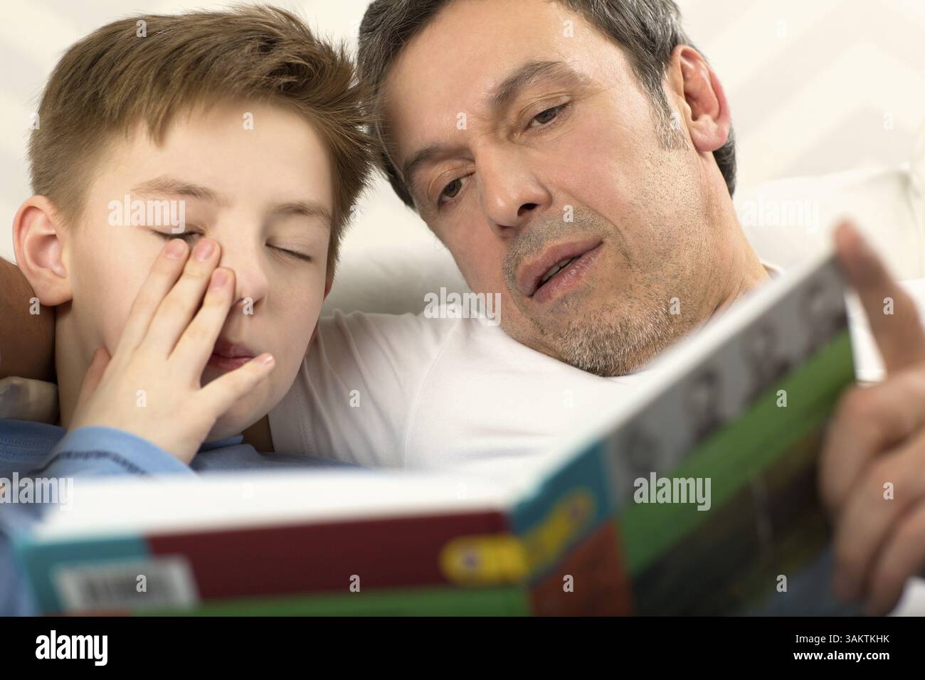 Close-up shot of a father reading a book to the son who is already ...
