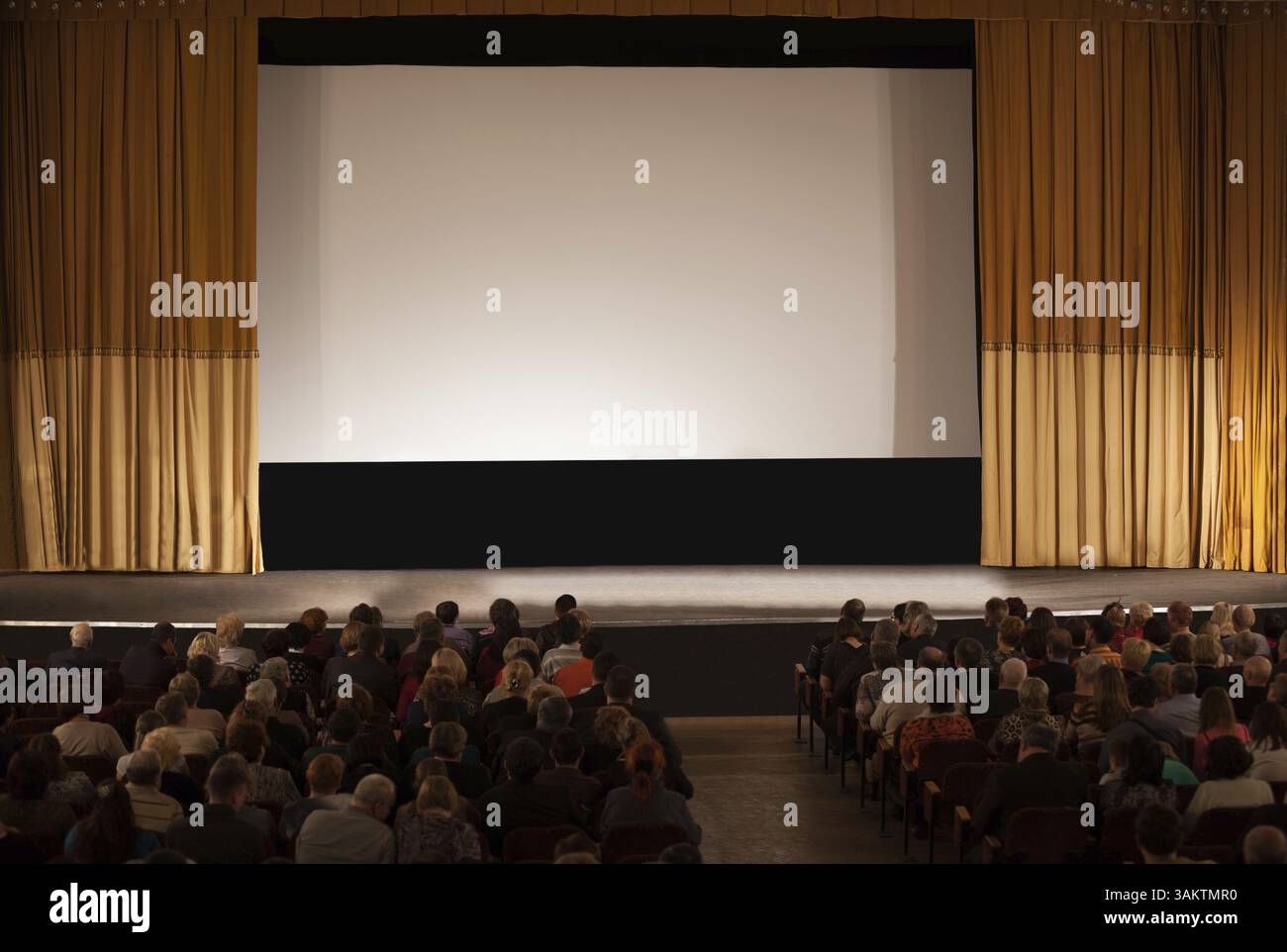 Audience seated in an auditorium in front of a stage with a screen and ...