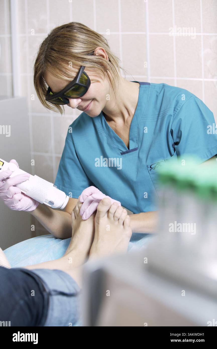 Podiatrist doing a foot laser treatment on a woman to kill fungal ...