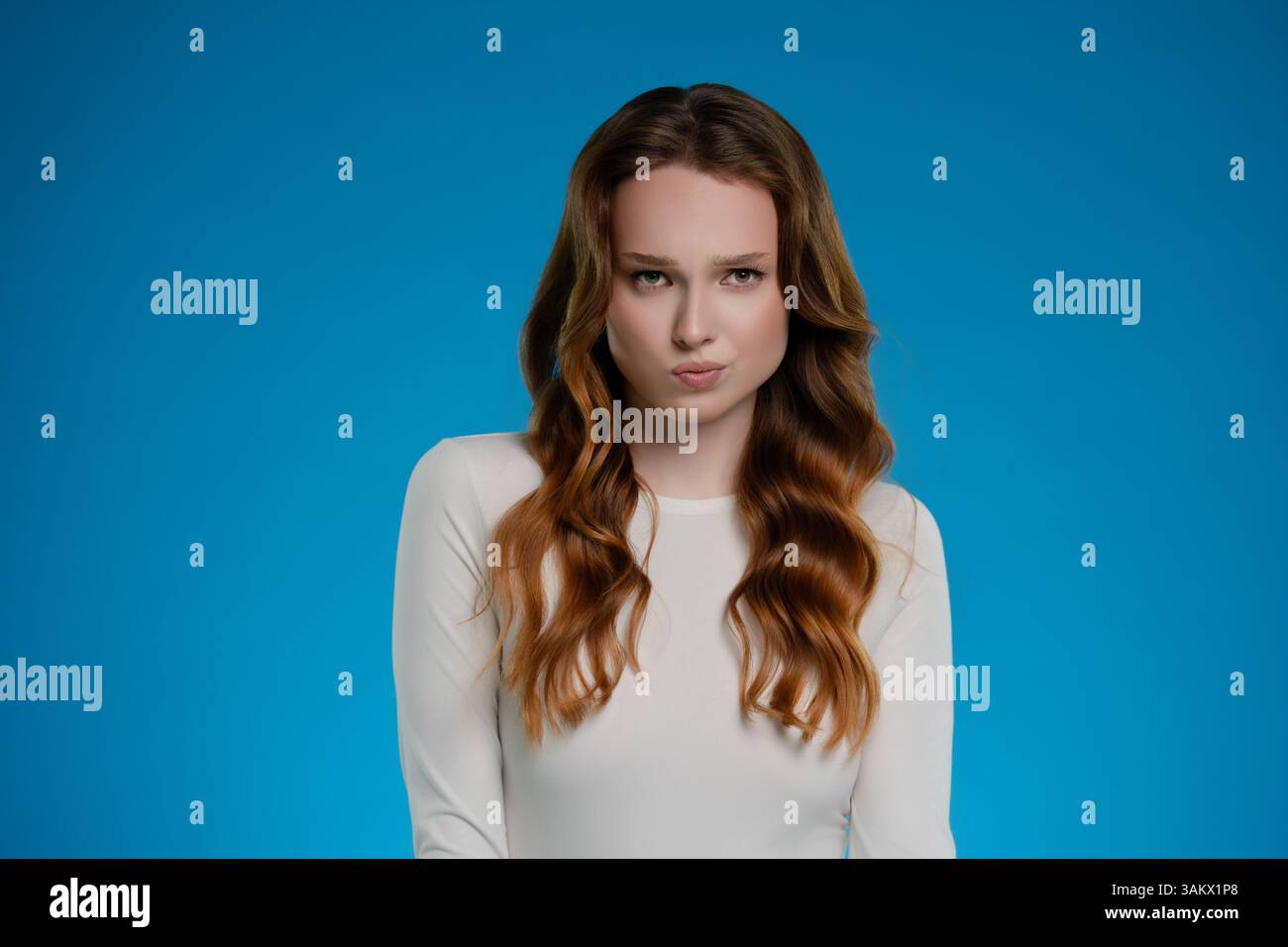 Woman posing in a studio setting with a blue background, expressing a ...