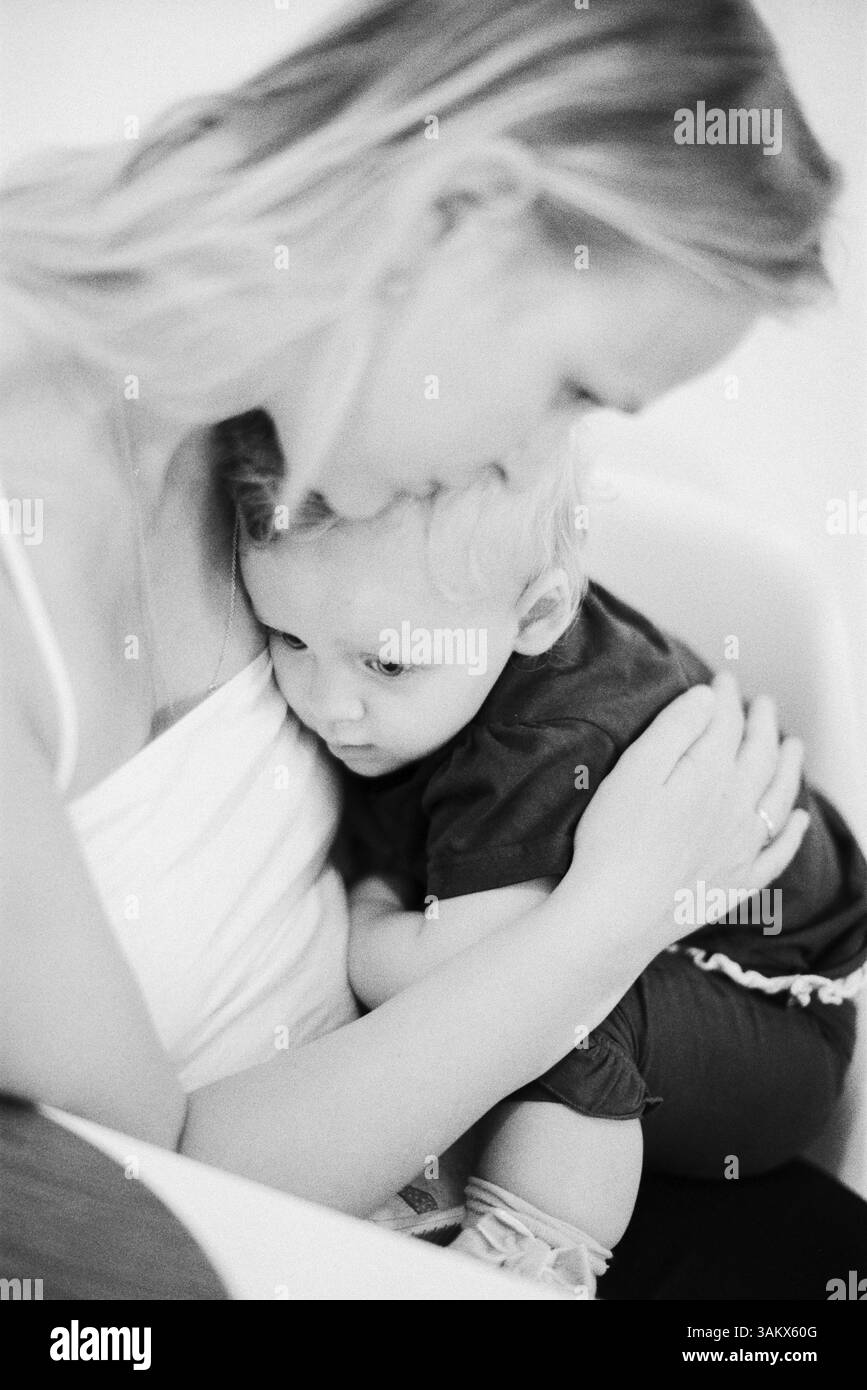Black and white shot of mother embracing one year old daughter sitting ...