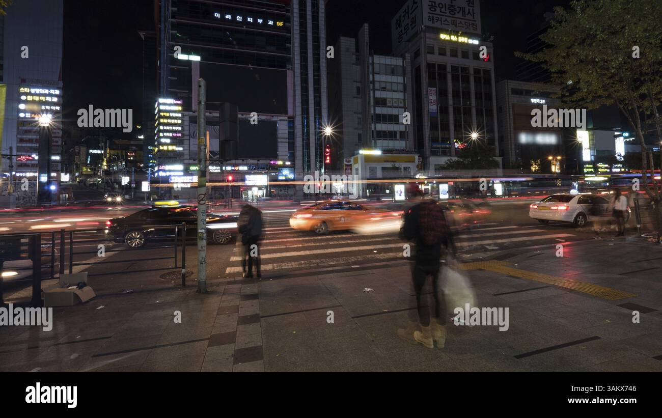 Road traffic and some pedestrians waiting at zebra crossing at night ...