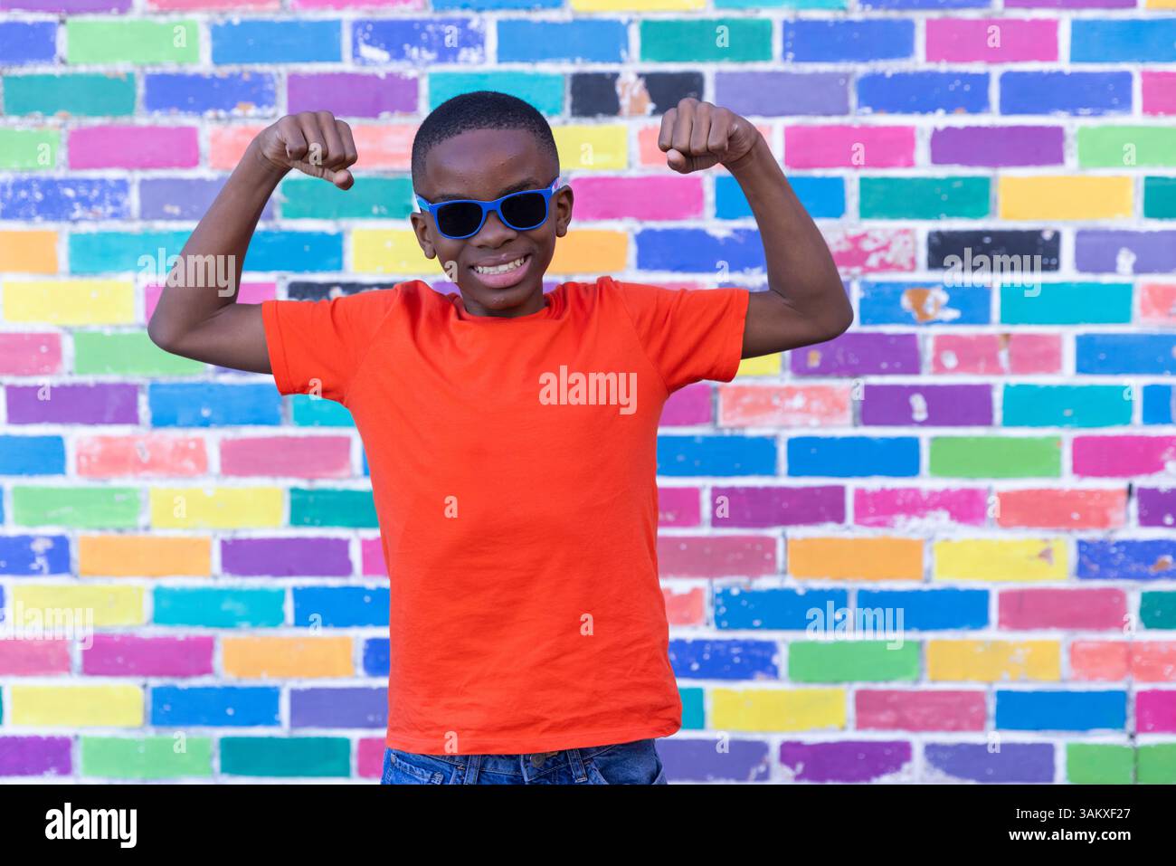 Smiling boy in sunglasses flexing muscles in front of colorful brick ...