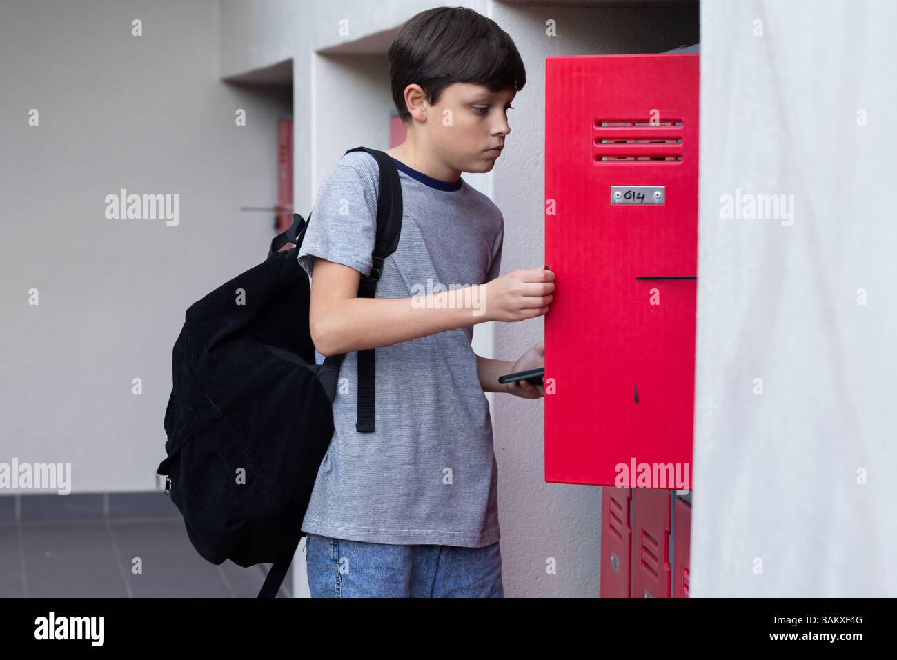Opening locker, boy with backpack holding smartphone in school hallway ...