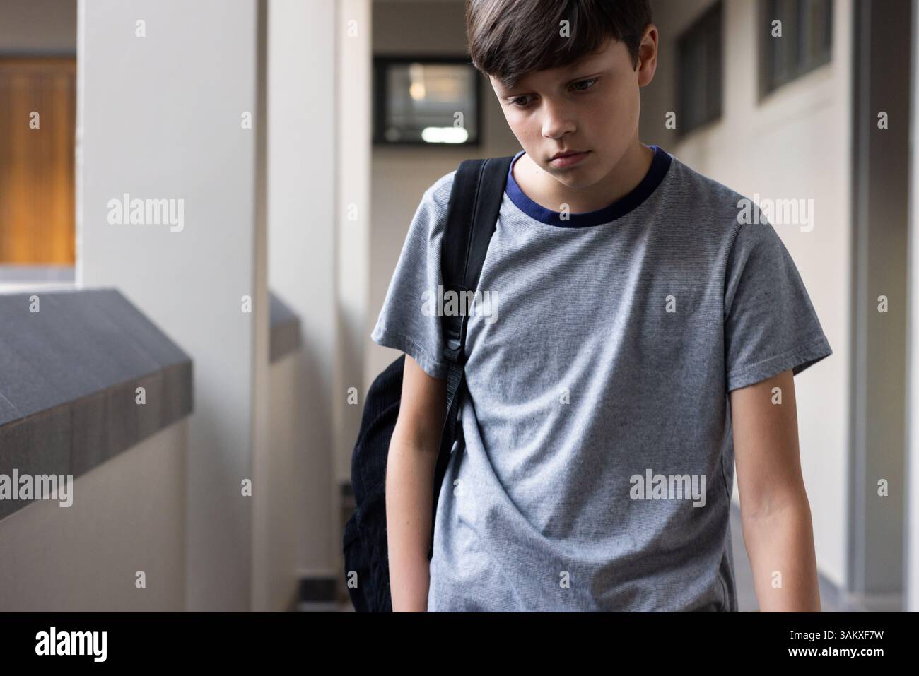 Walking in school hallway, boy with backpack looking down, feeling sad ...