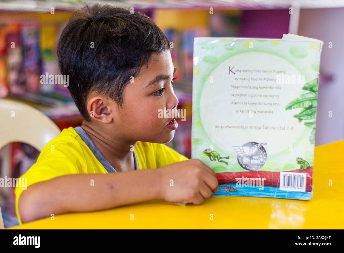 A young Filipino student reading a children's book inside a public ...