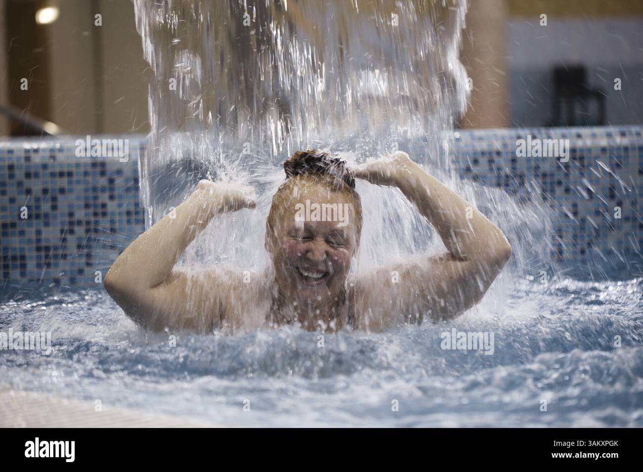 Overweight middle-aged woman playing under a water fountain splashing ...