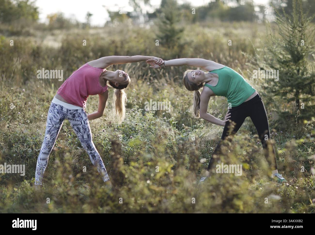Two supple athletic young women working out together in the countryside ...