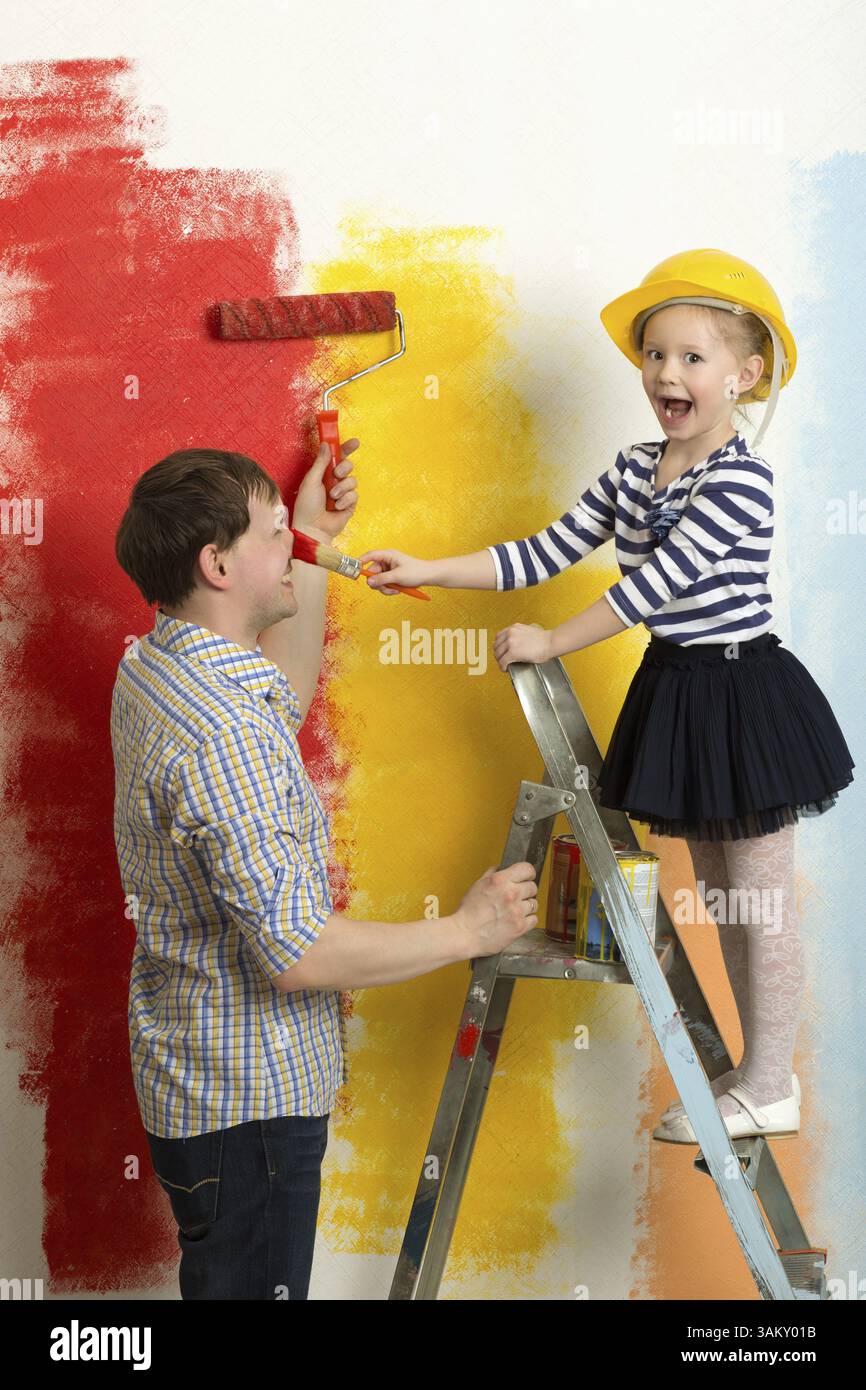Girl and father fooling while painting wall in bright colours. Girl in ...