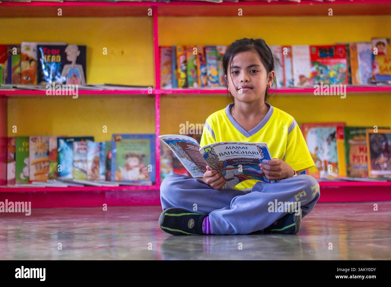 A young Filipino student reading a children's book inside a public ...