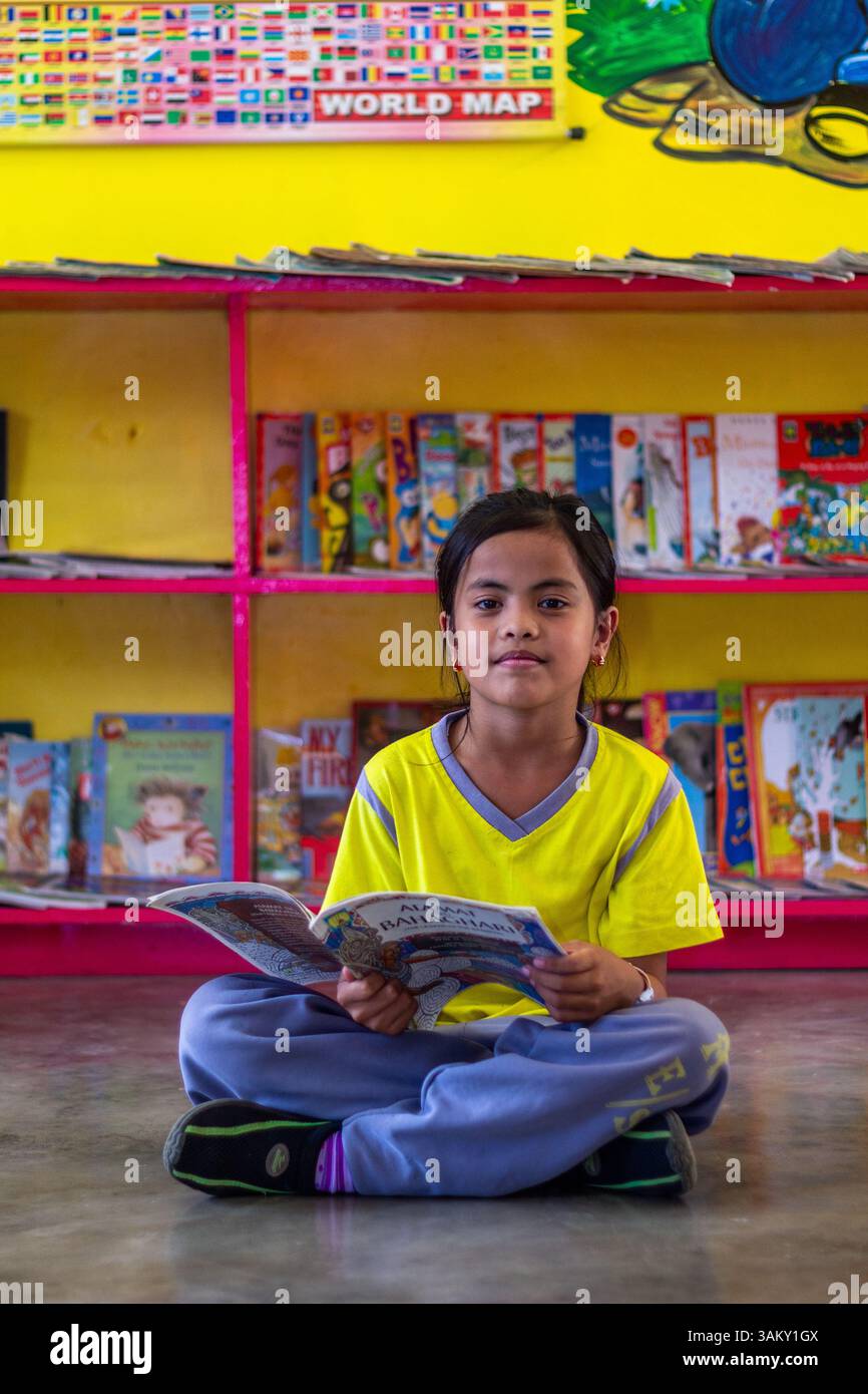 A young Filipino student reading a children's book inside a public ...
