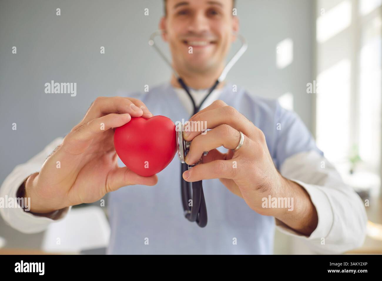 Male doctor cardiologist with stethoscope examining red heart standing ...