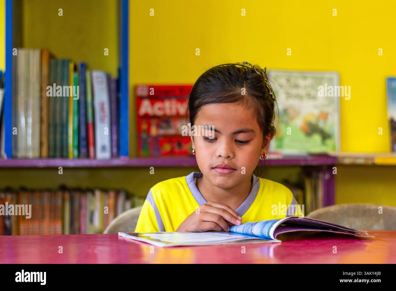 A young Filipino student reading a children's book inside a public ...