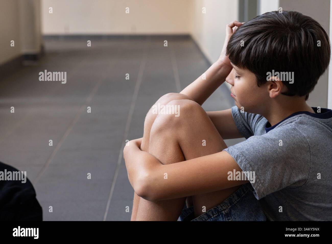 Sitting alone in school hallway, boy looking down and thinking deeply ...