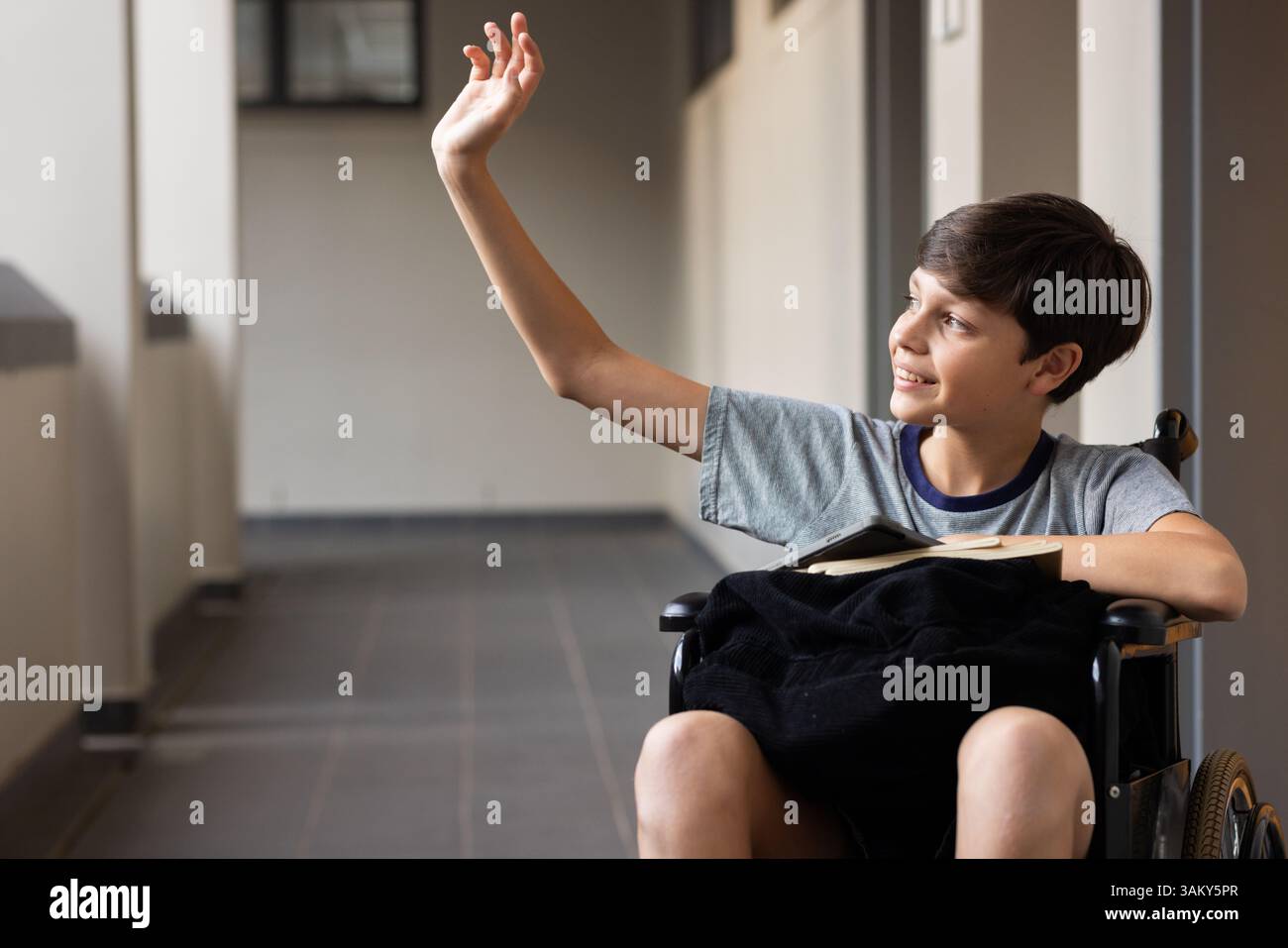 In school, boy in wheelchair waving and smiling in hallway Stock Photo ...