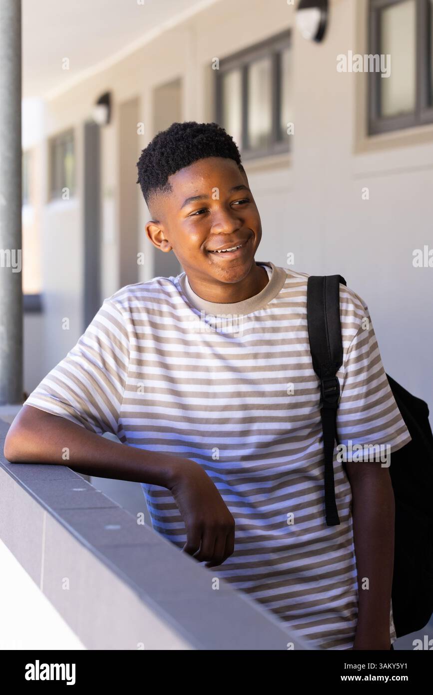 Smiling student with backpack leaning on railing in school hallway ...