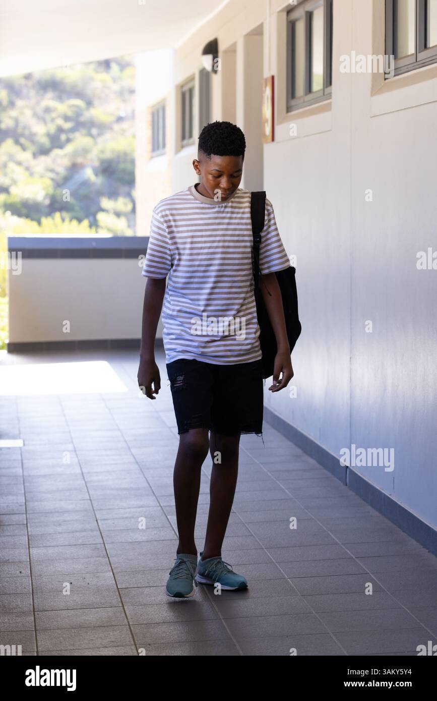 Walking in school hallway, boy carrying backpack and looking down Stock ...