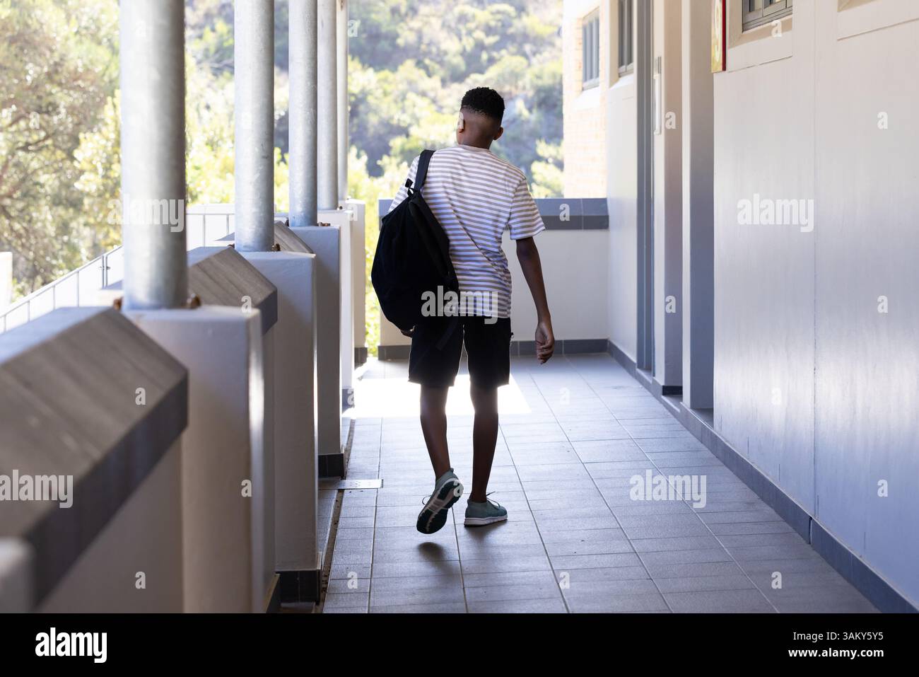 Walking down school hallway, boy carrying backpack and wearing striped ...