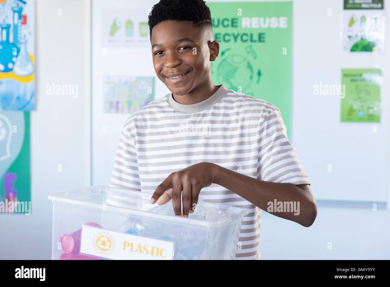 Recycling plastic, boy smiling and holding bin in school classroom ...