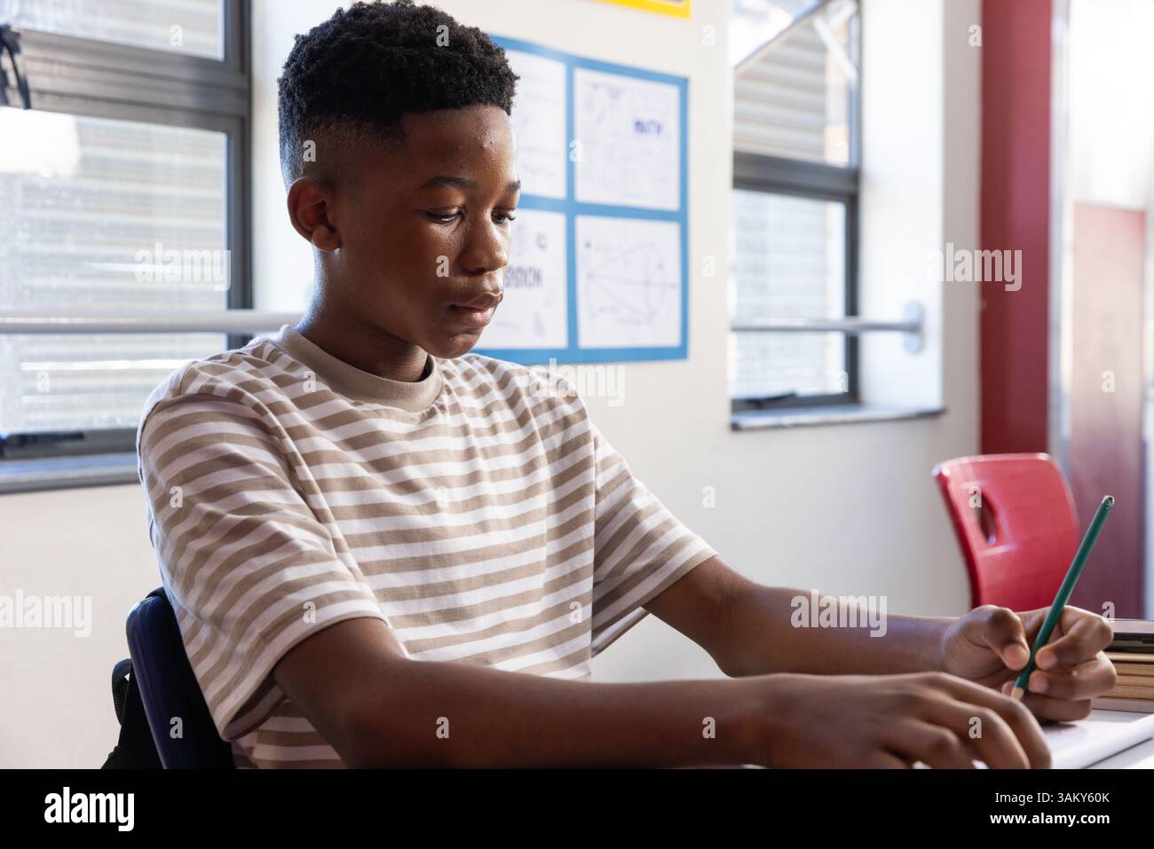 In school, boy concentrating while writing with pencil in classroom ...