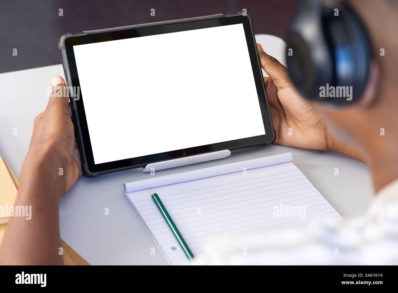Using tablet with headphones, student taking notes in school classroom ...