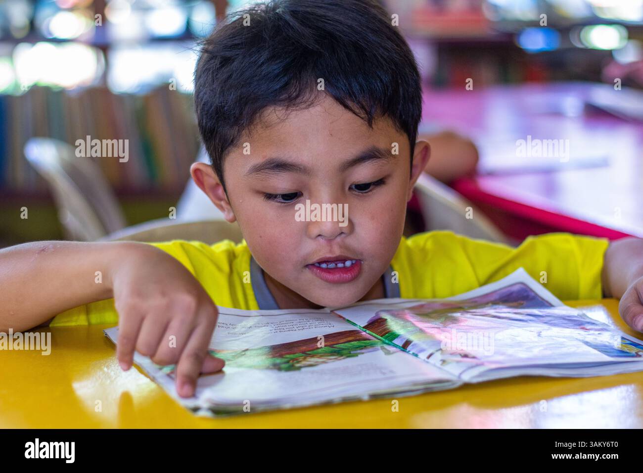 A young Filipino student reading a children's book inside a public ...