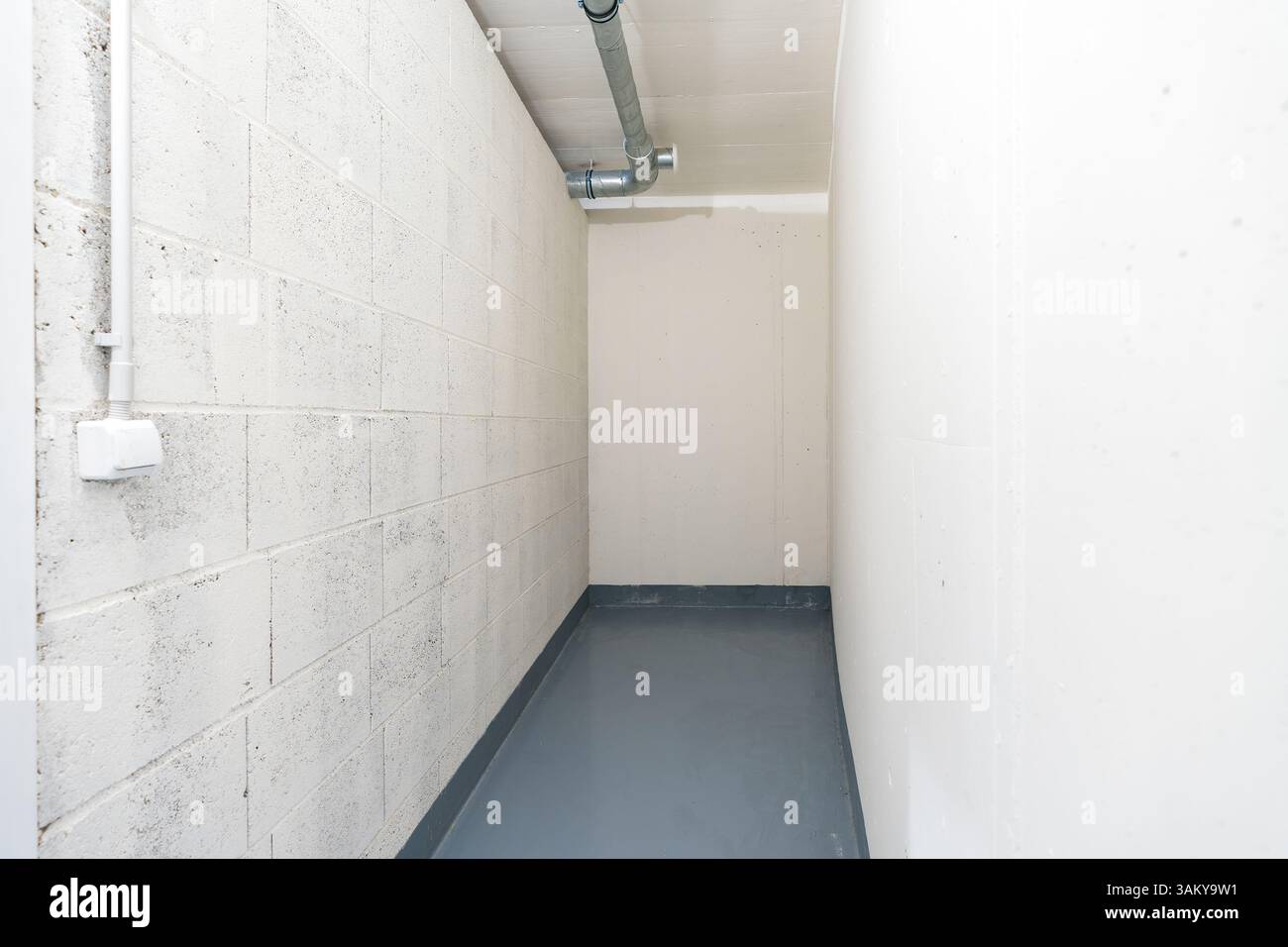 Small utility storage room with ventilation pipe and concrete walls ...