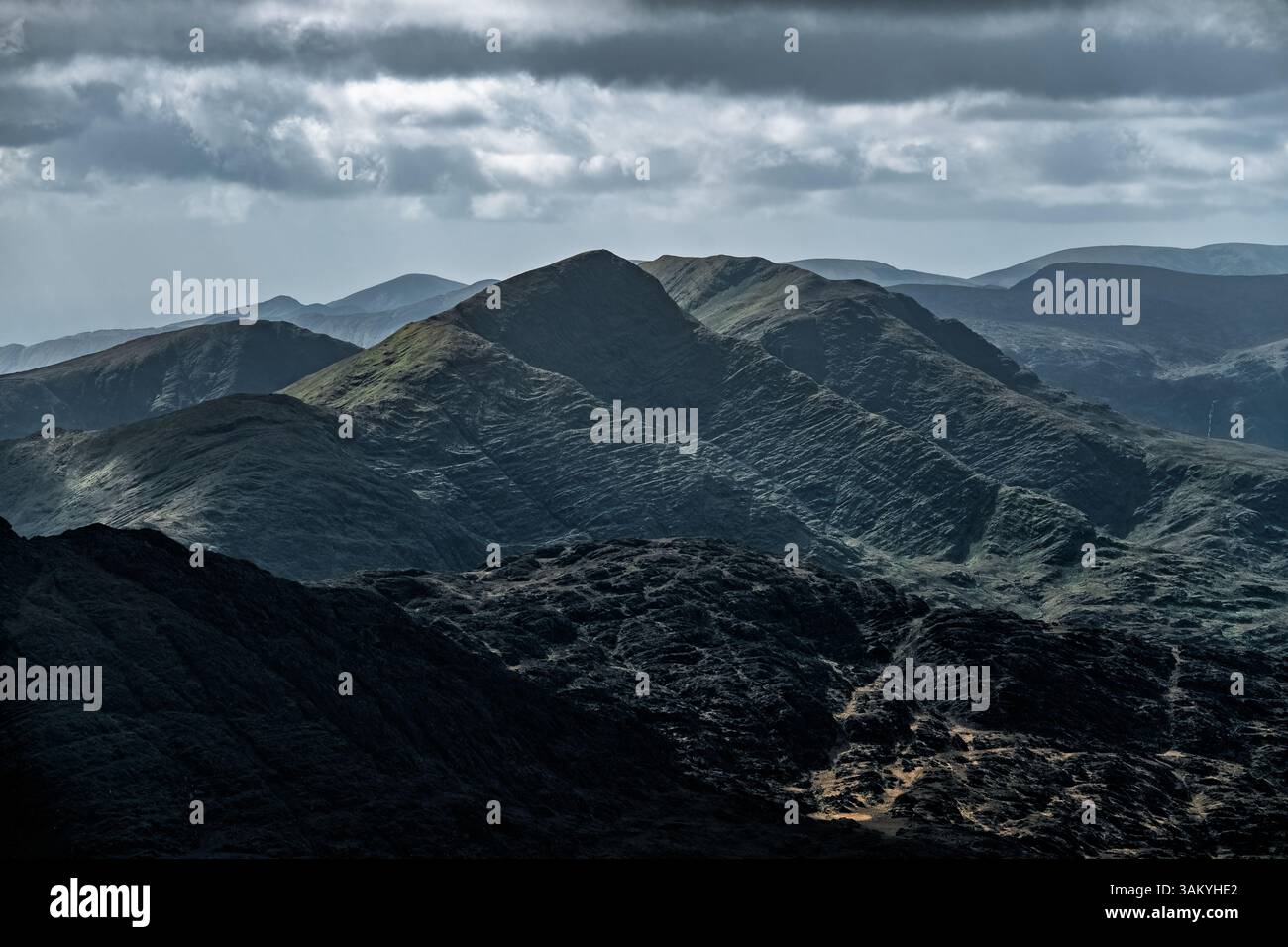 Dark, rolling hills under a cloudy sky. Shadows accentuate the rugged ...