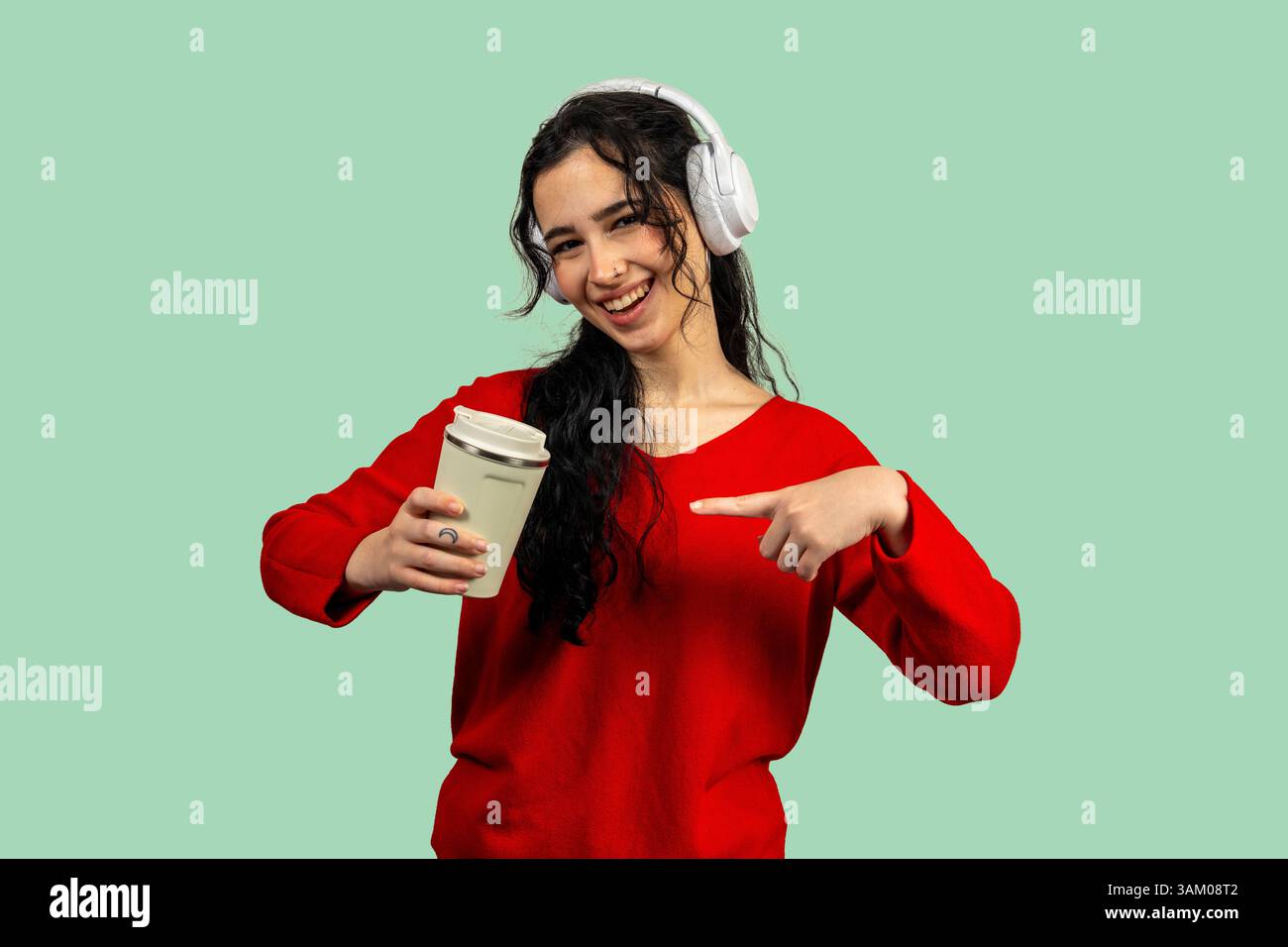 Happy young woman pointing at reusable coffee cup while listening to ...
