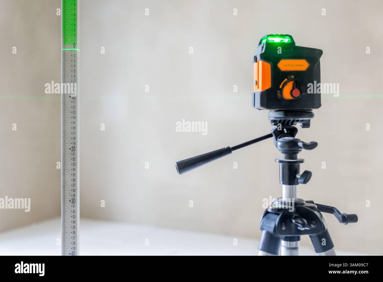 Laser level on tripod projecting green beam onto ruler in empty room ...