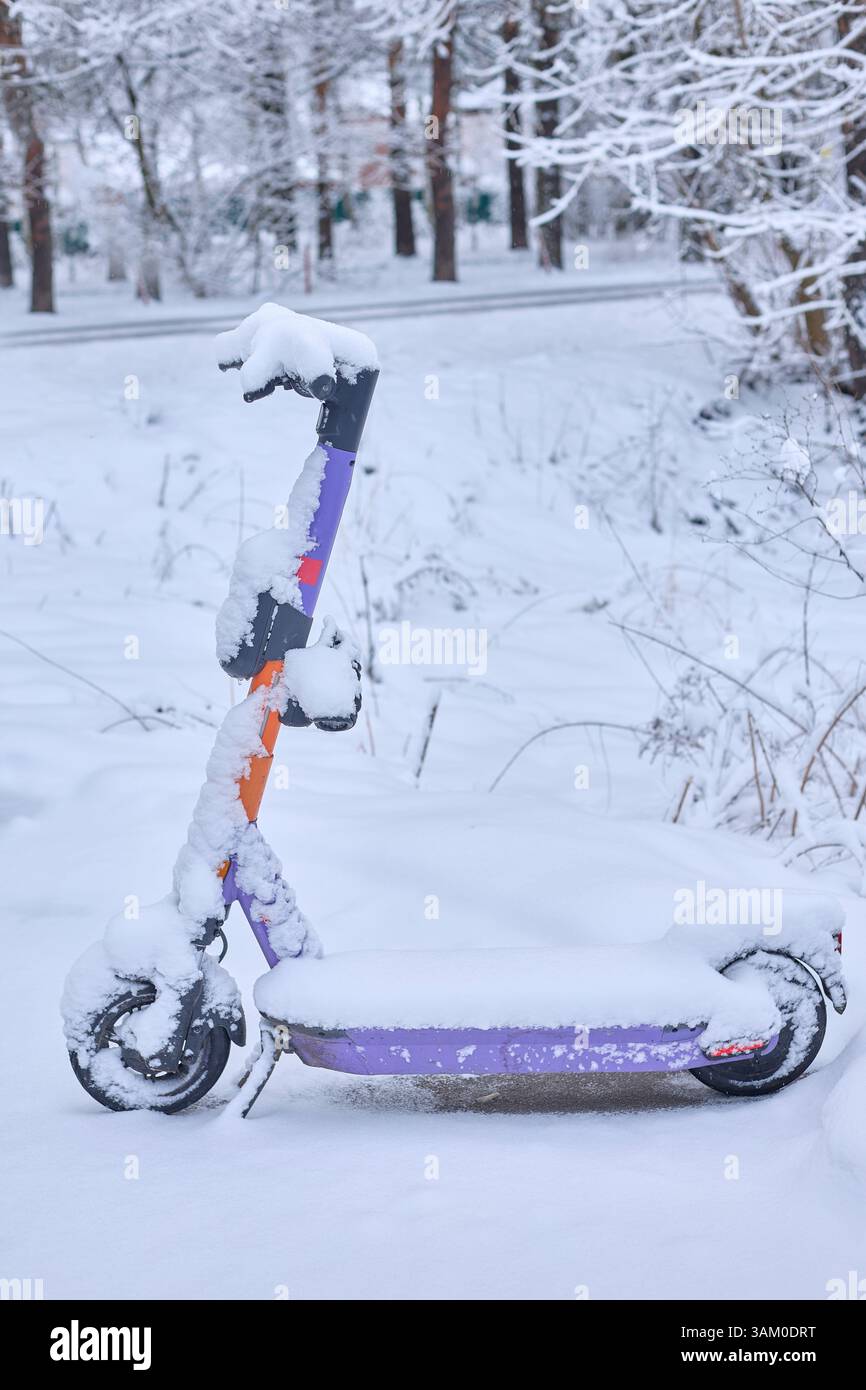 A discarded electric scooter, blanketed by heavy snowfall, illustrates ...