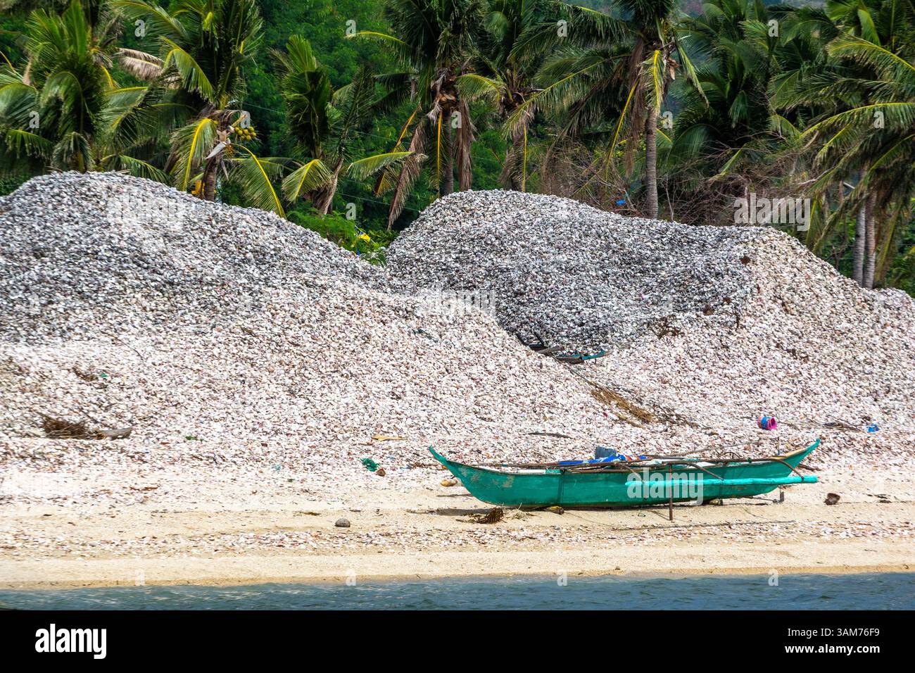 A lone banca docked on the shore with piles of empty scallop shells in ...
