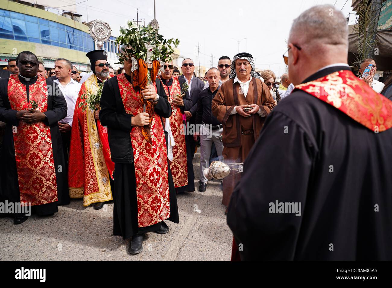 Al Hamdaniya, Iraq. 13th Apr, 2025. A priest carries a cross decorated ...